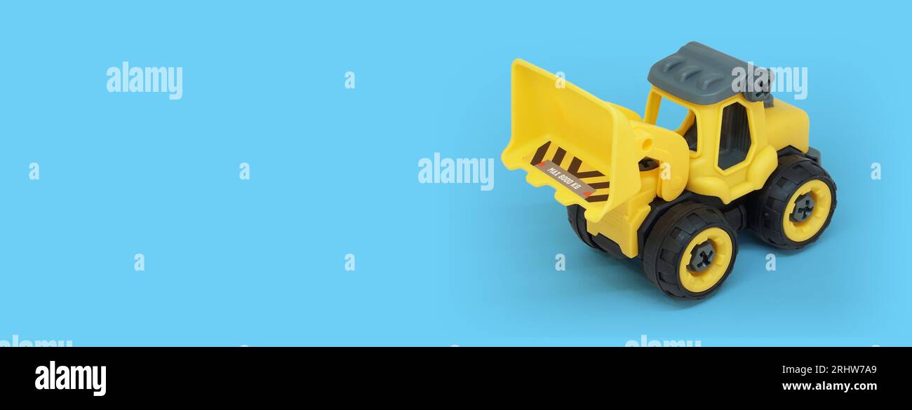 yellow plastic bulldozer toy isolated on blue background with copy ...
