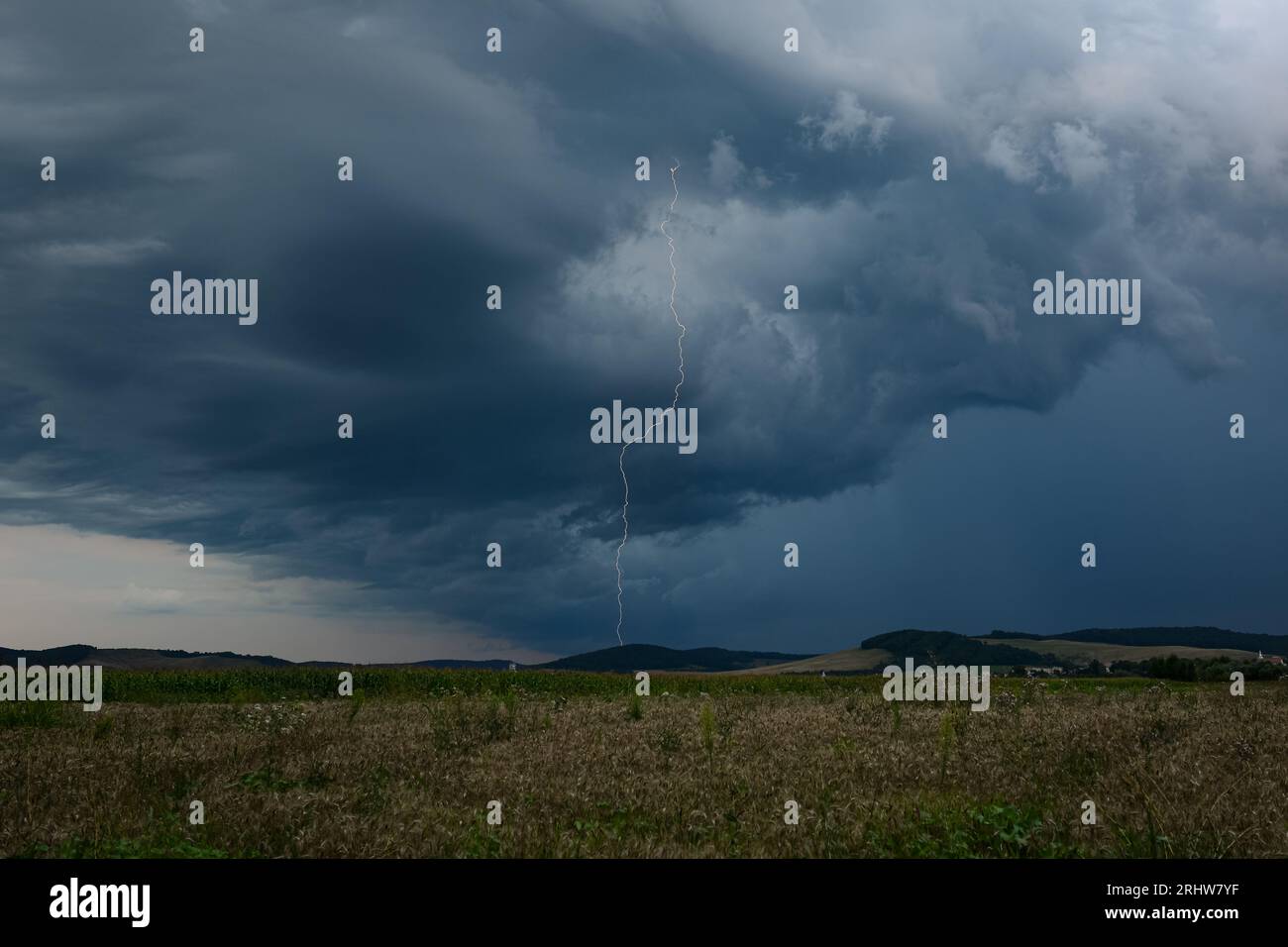 Narrow long vertical lightning bolt shoots out of a dark thundercloud ...