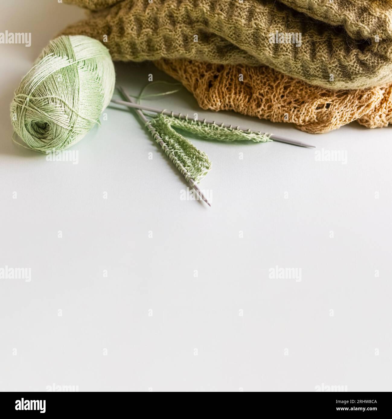 Green yarn thread with knitting needles and finished yarn products on a ...