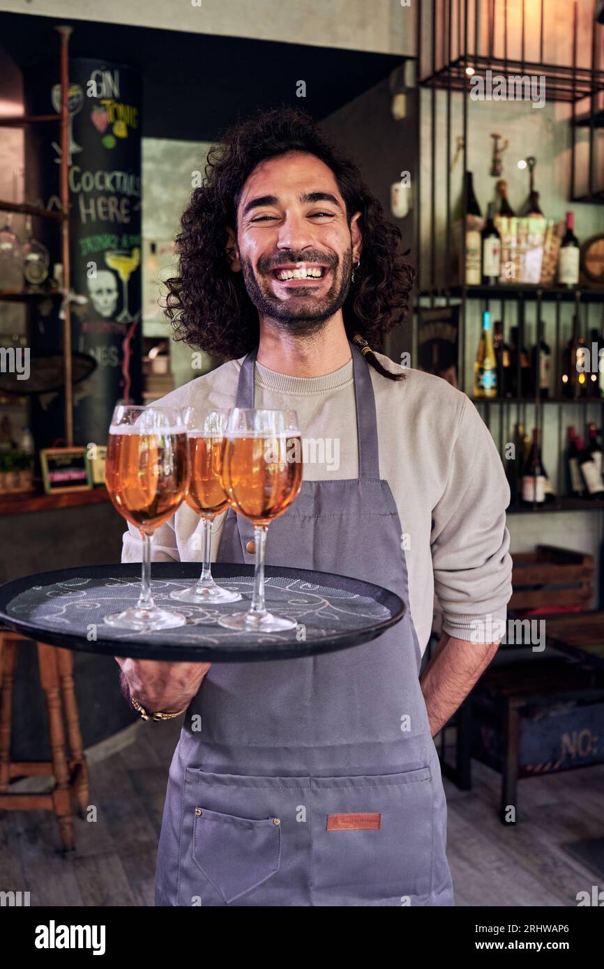 Cheerful waiter looking at camera while holding a tray with beers at ...