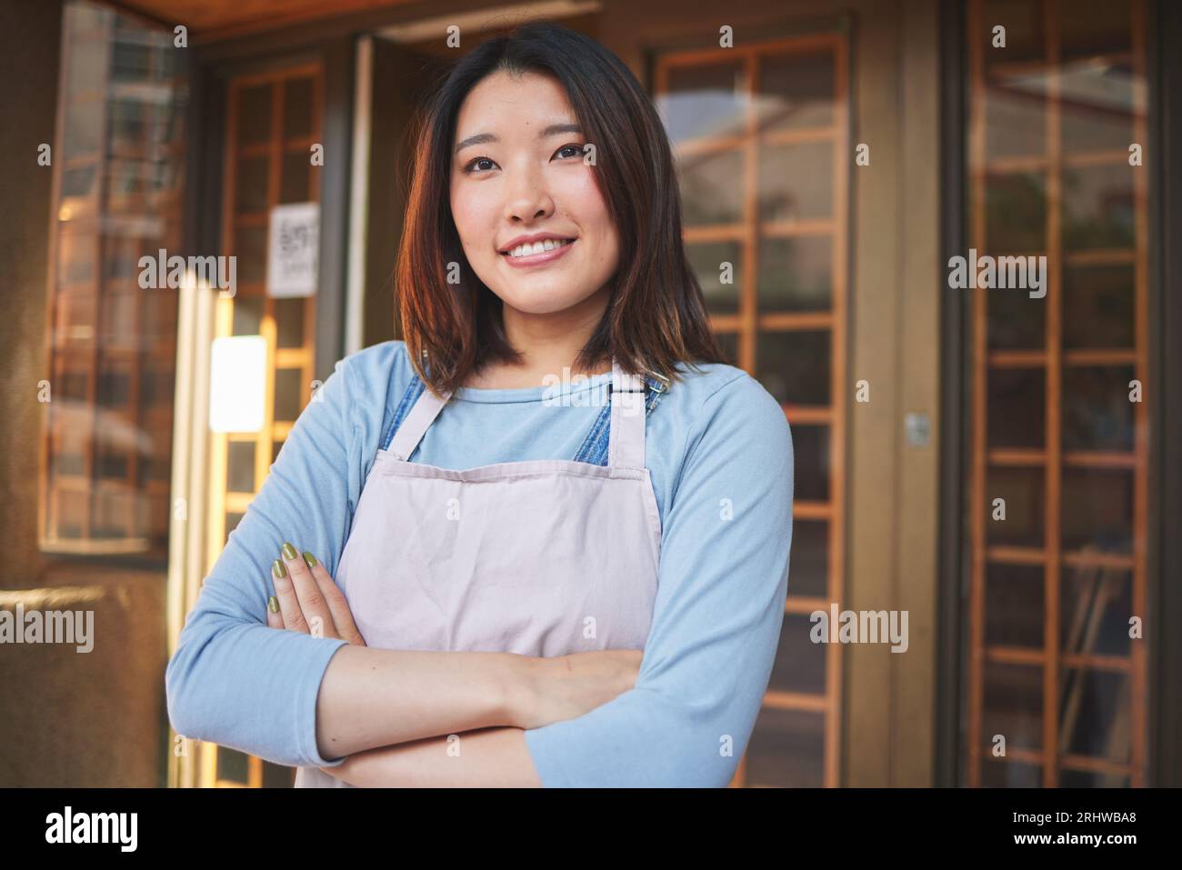 Happy, waitress and Asian woman with arms crossed at restaurant, coffee shop or startup store ...