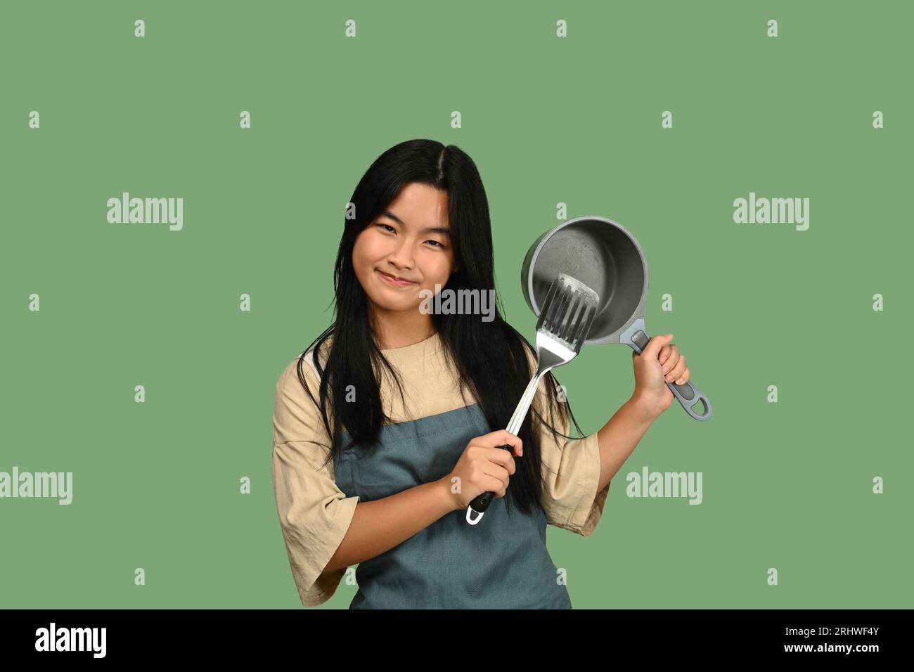 Playful teenage girl wearing apron holding pan and spatula isolated on ...