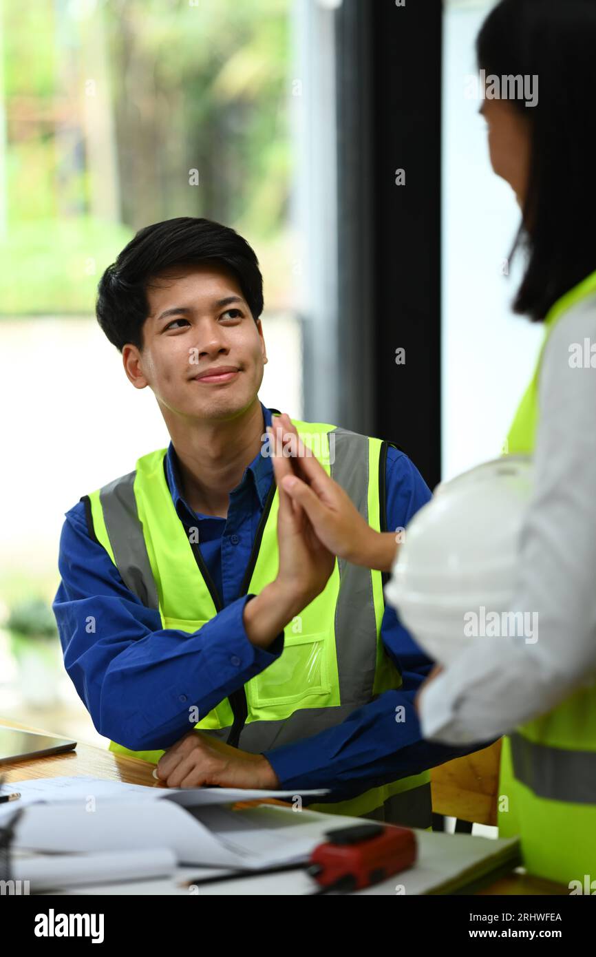 Smiling civil engineer man giving high five with colleague, celebrating ...