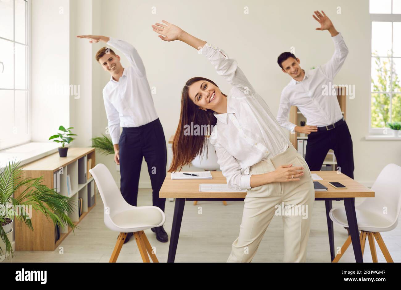 Happy smiling young business people doing stretching exercises in ...