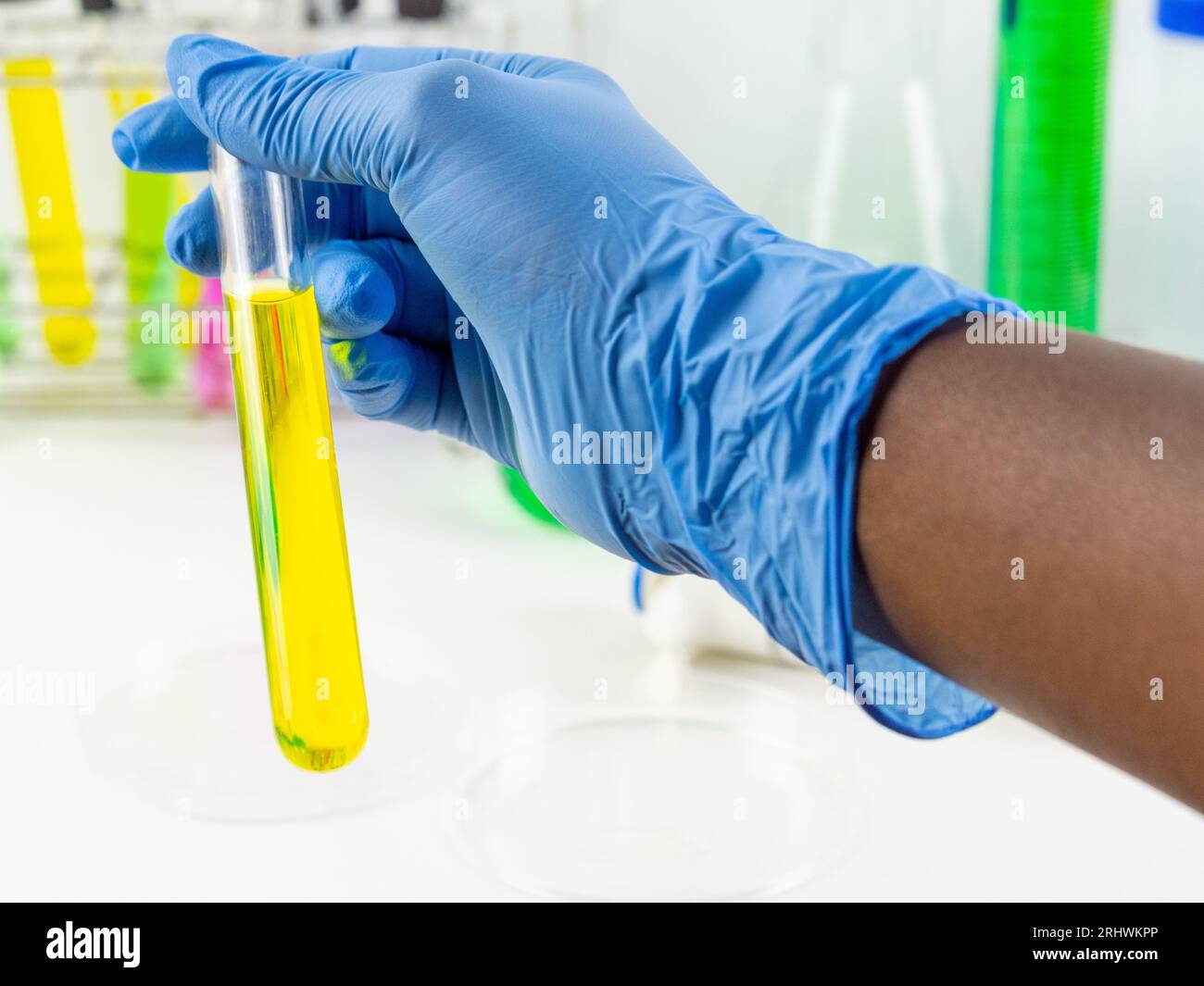 A close up of a hand wearing gloves holding a test tube with different ...
