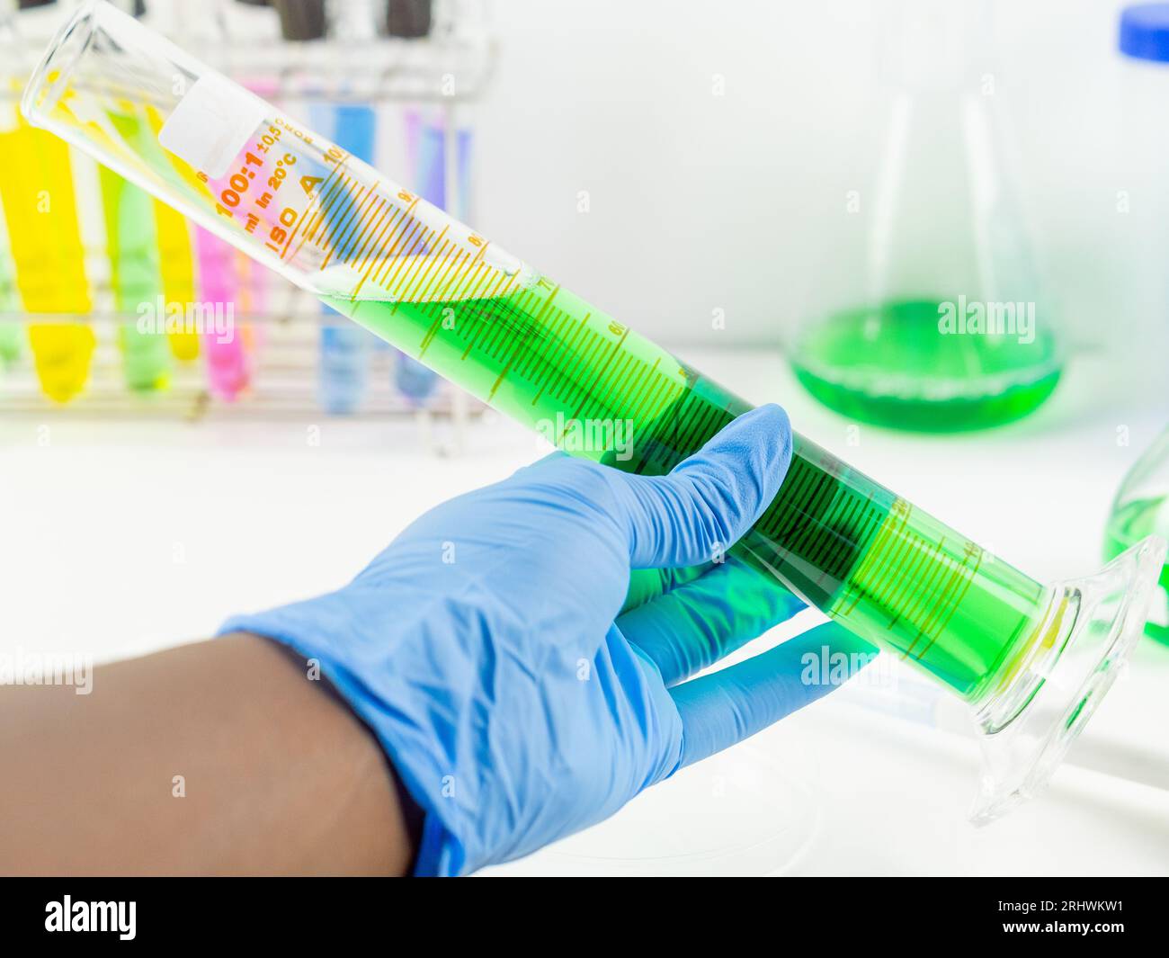 A close up of a female hand holding a measuring cylinder with a green ...