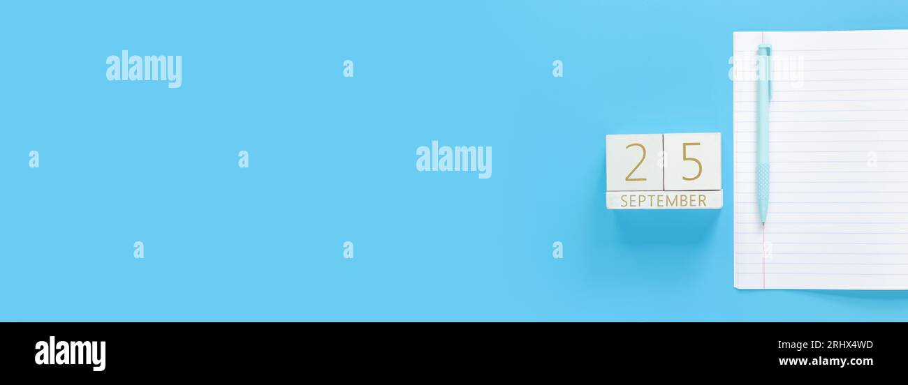 25 September. Wooden calendar on a blue background with an open notepad ...