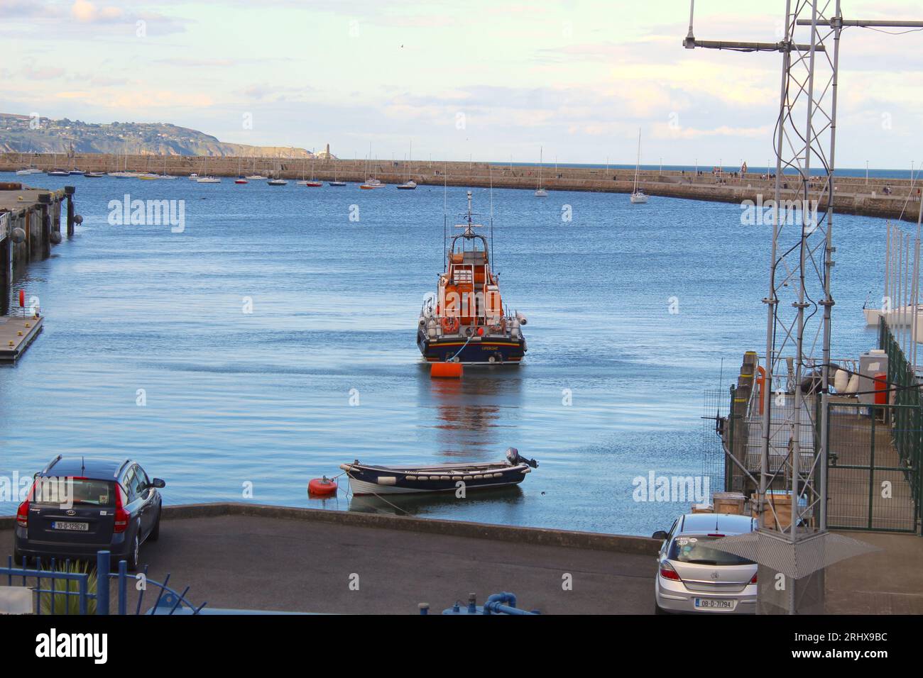 A photo of an orange boat leaving a harbour on during a sunny evening ...