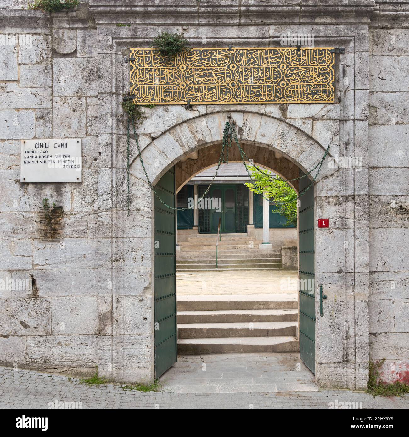 Arched entrance with open green metal door in brick stone wall leading ...