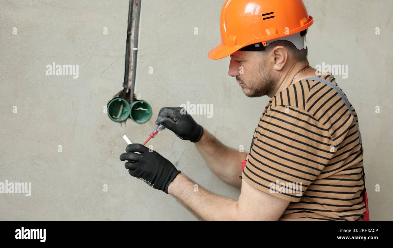 Electrician male in uniform, protective gloves and helmet checks ...