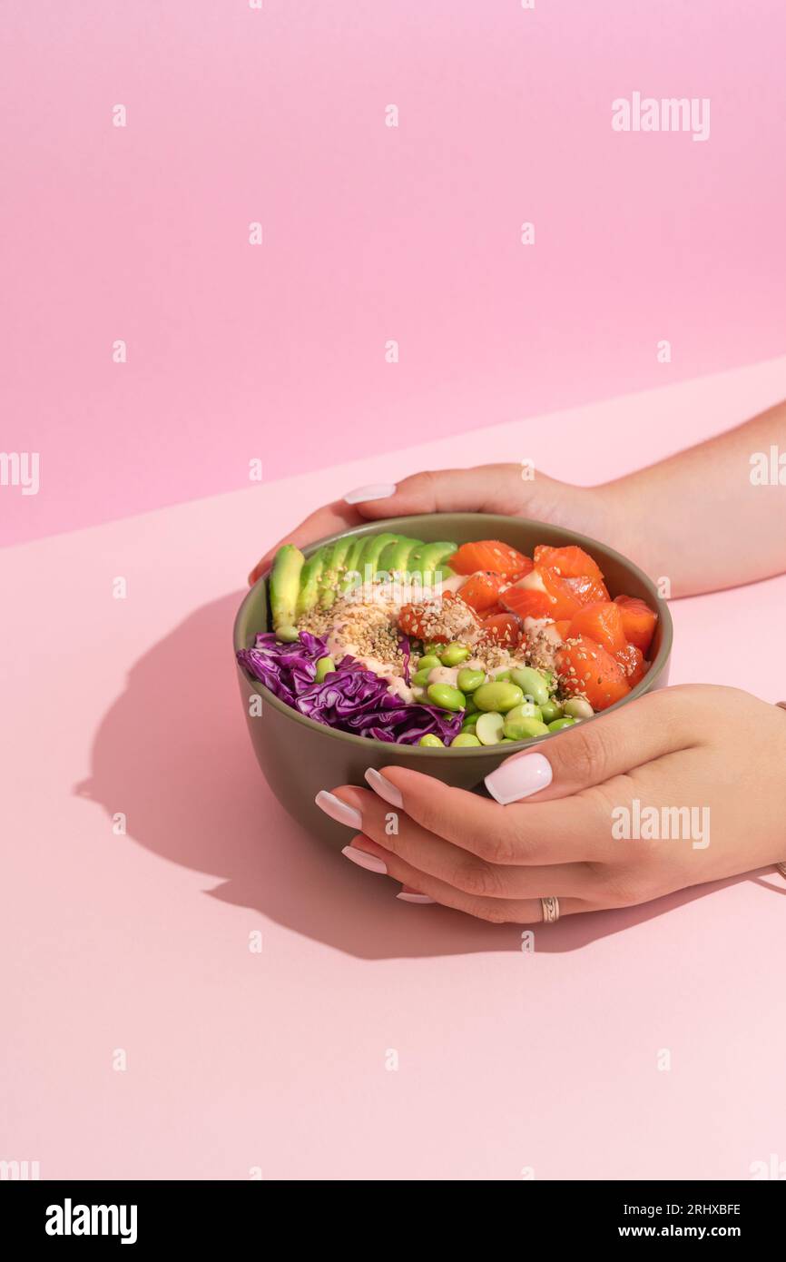 Hand with poke bowl with salmon on pink background Stock Photo - Alamy