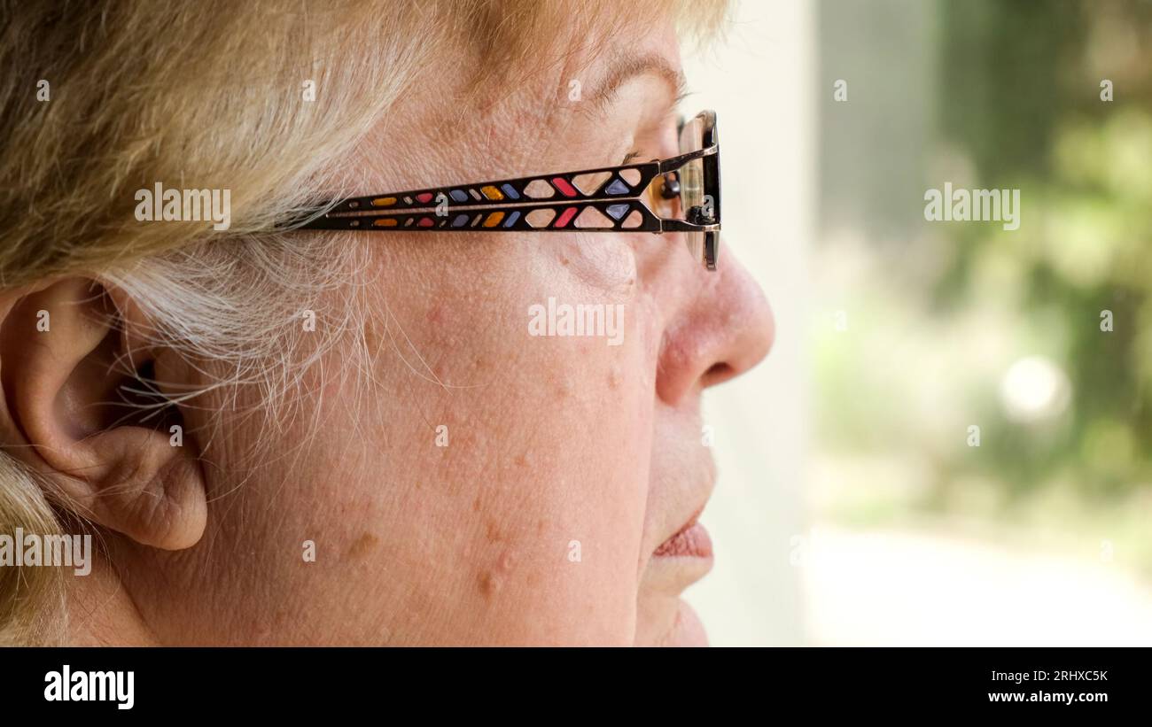 Old woman in glasses looking at the window. Profile face of grandmother ...