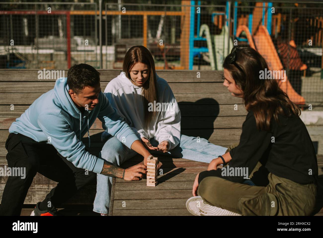 Three friends playing jenga while sitting on the wooden bench at the ...