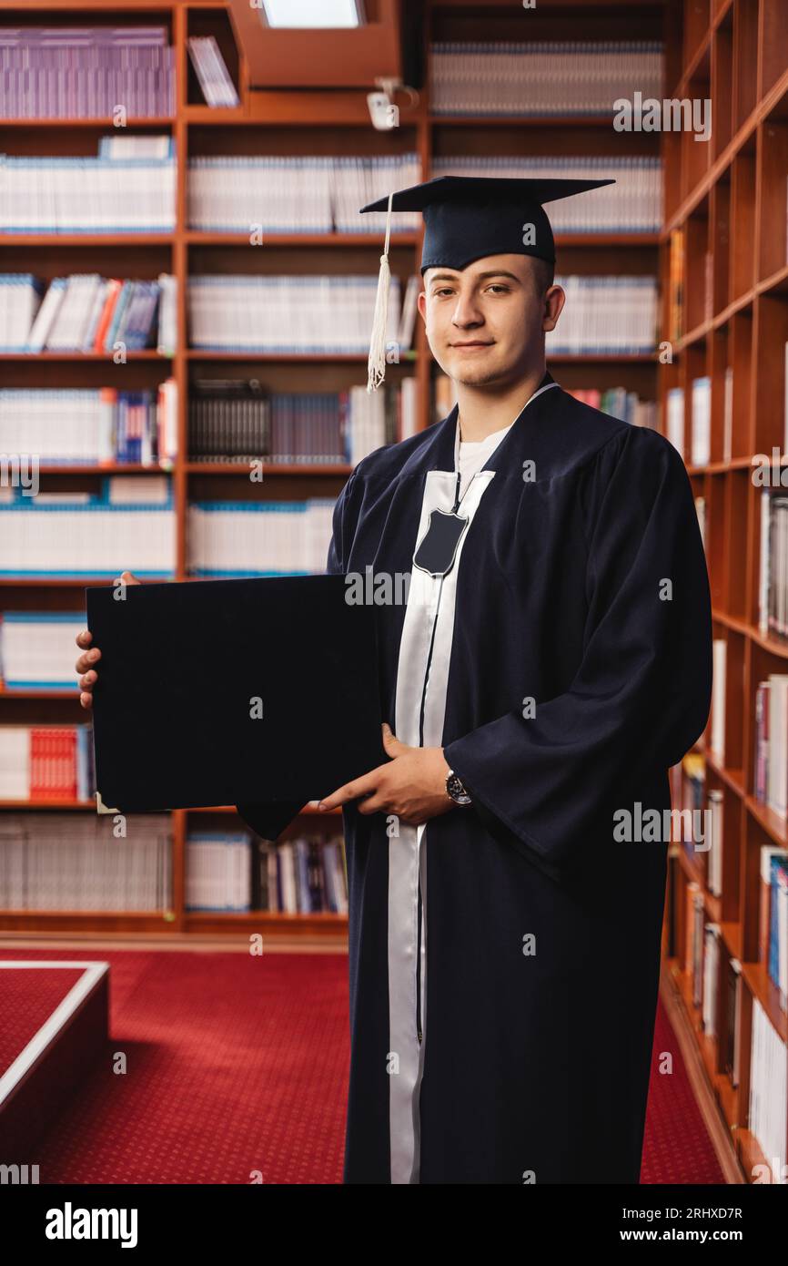 Young and happy graduate wearing a cap and gown and holding his ...