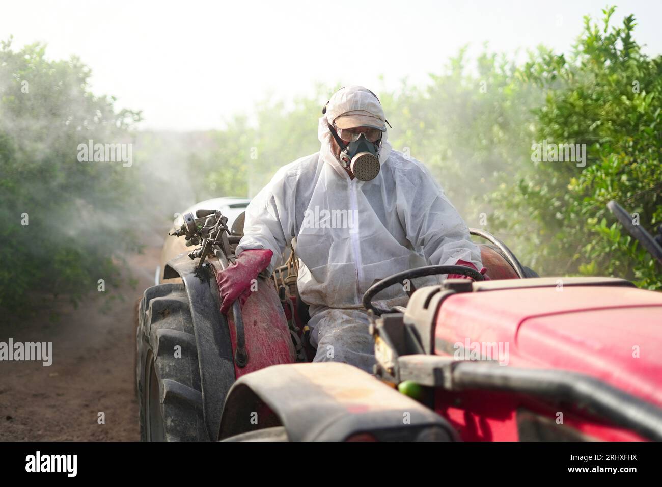 Anonymous farmer wearing protective suit and mask spraying pesticide ...