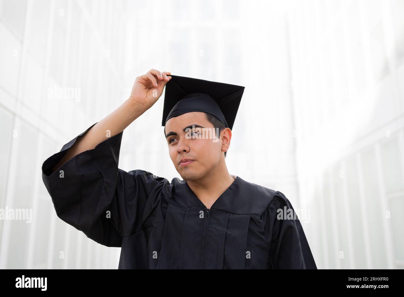 Portrait of confident handsome young man wearing black graduation gown ...