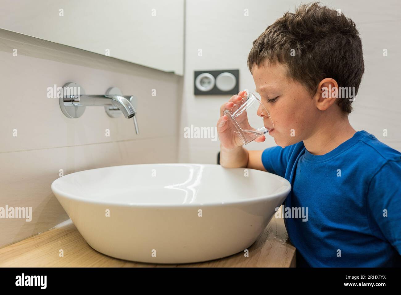 Side view cute boy in casual wear rinsing the mouth with a glass of ...