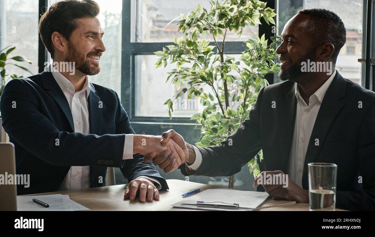 Two successful diverse businessmen sit at office desk with laptop happy ...