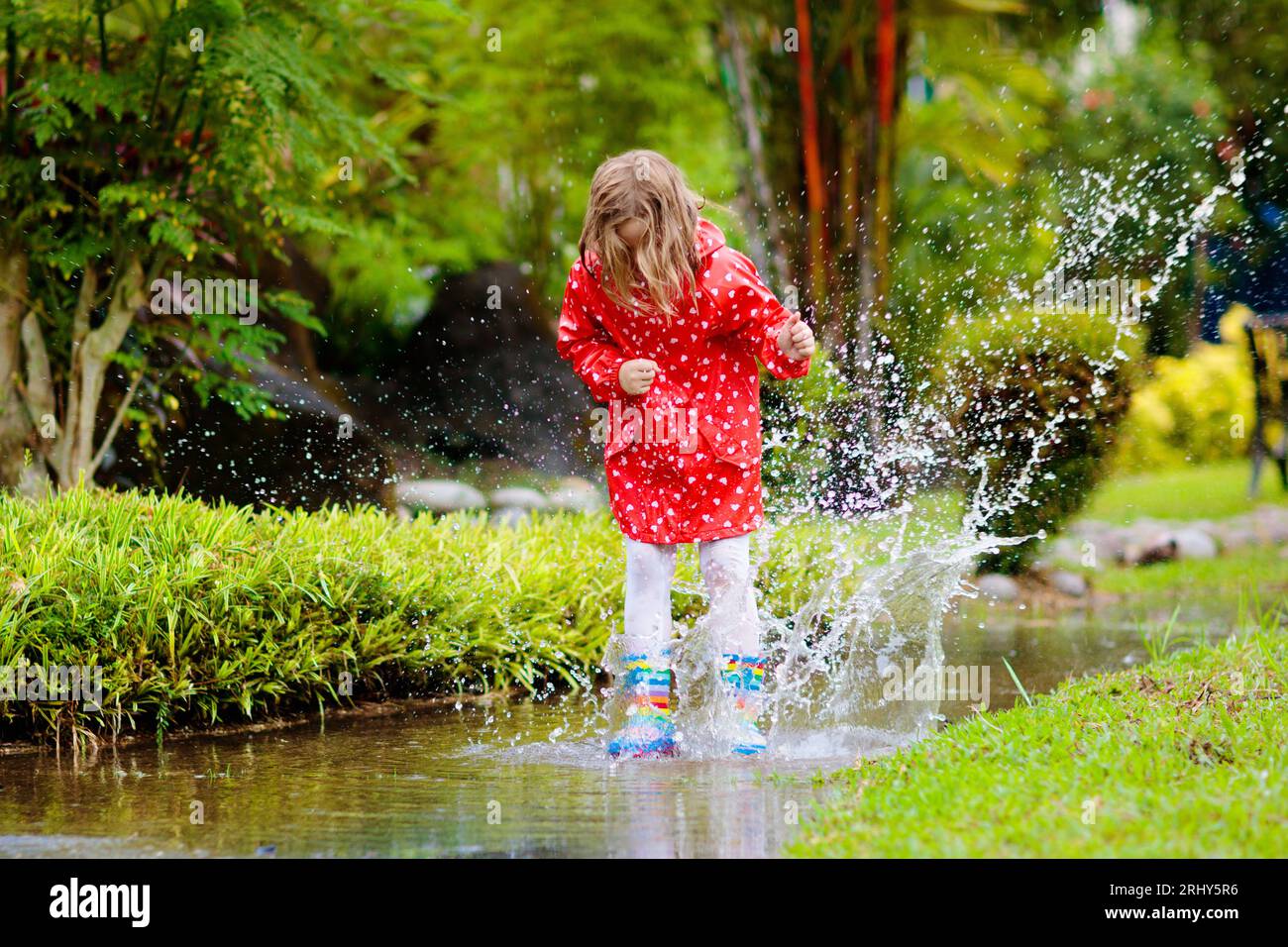 Child playing in puddle. Kids play and jump outdoor by autumn rain ...