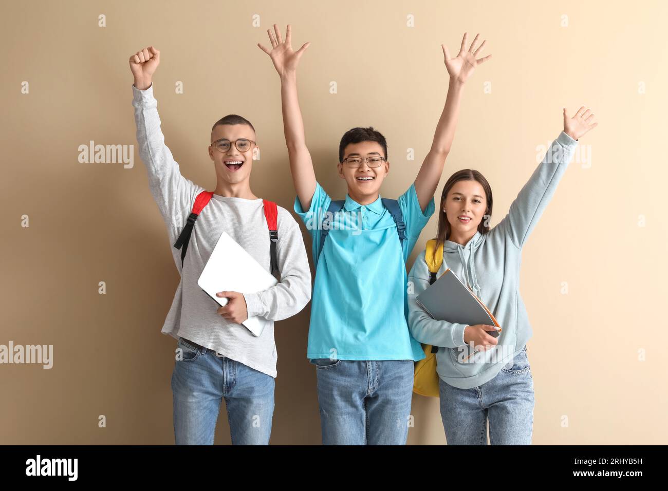 Happy students with backpacks, notebooks and laptop on beige background ...