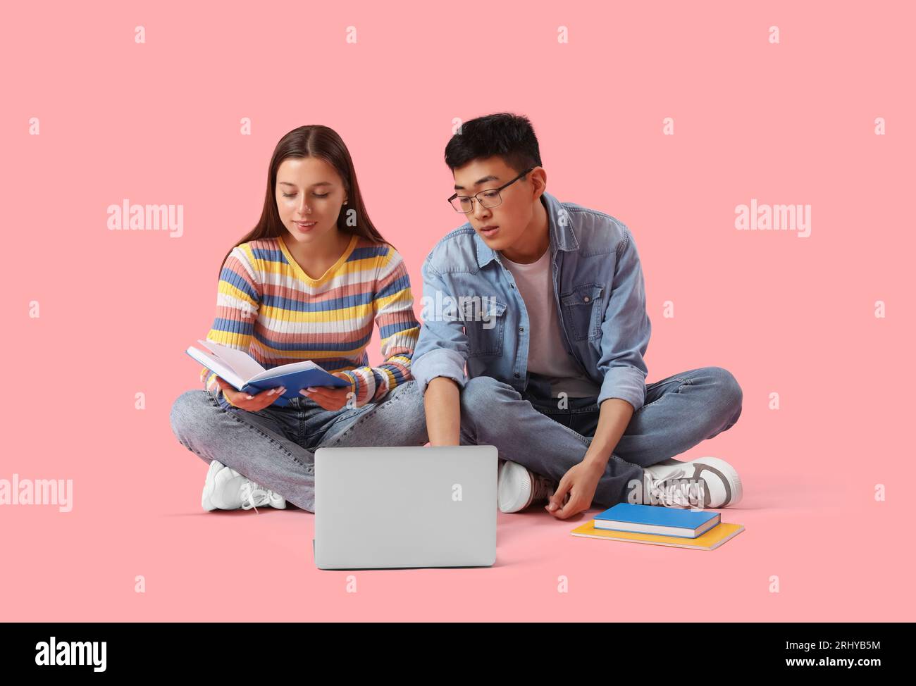 Happy students with books sitting on pink background and using laptop ...