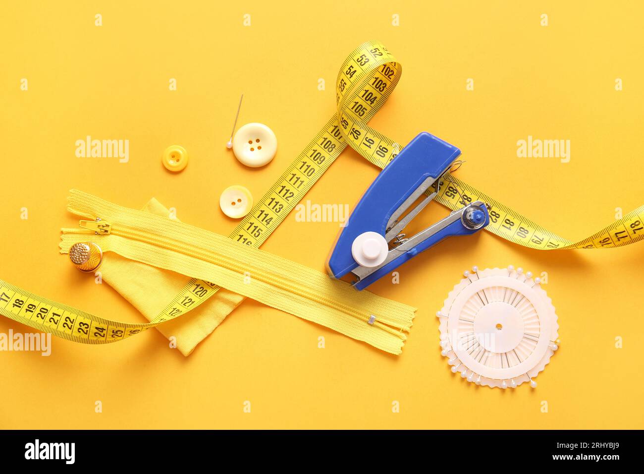 Manual sewing machine with different supplies on yellow background ...
