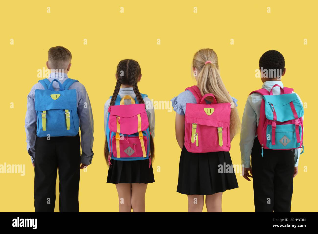 Little classmates in stylish uniform with backpacks on yellow ...