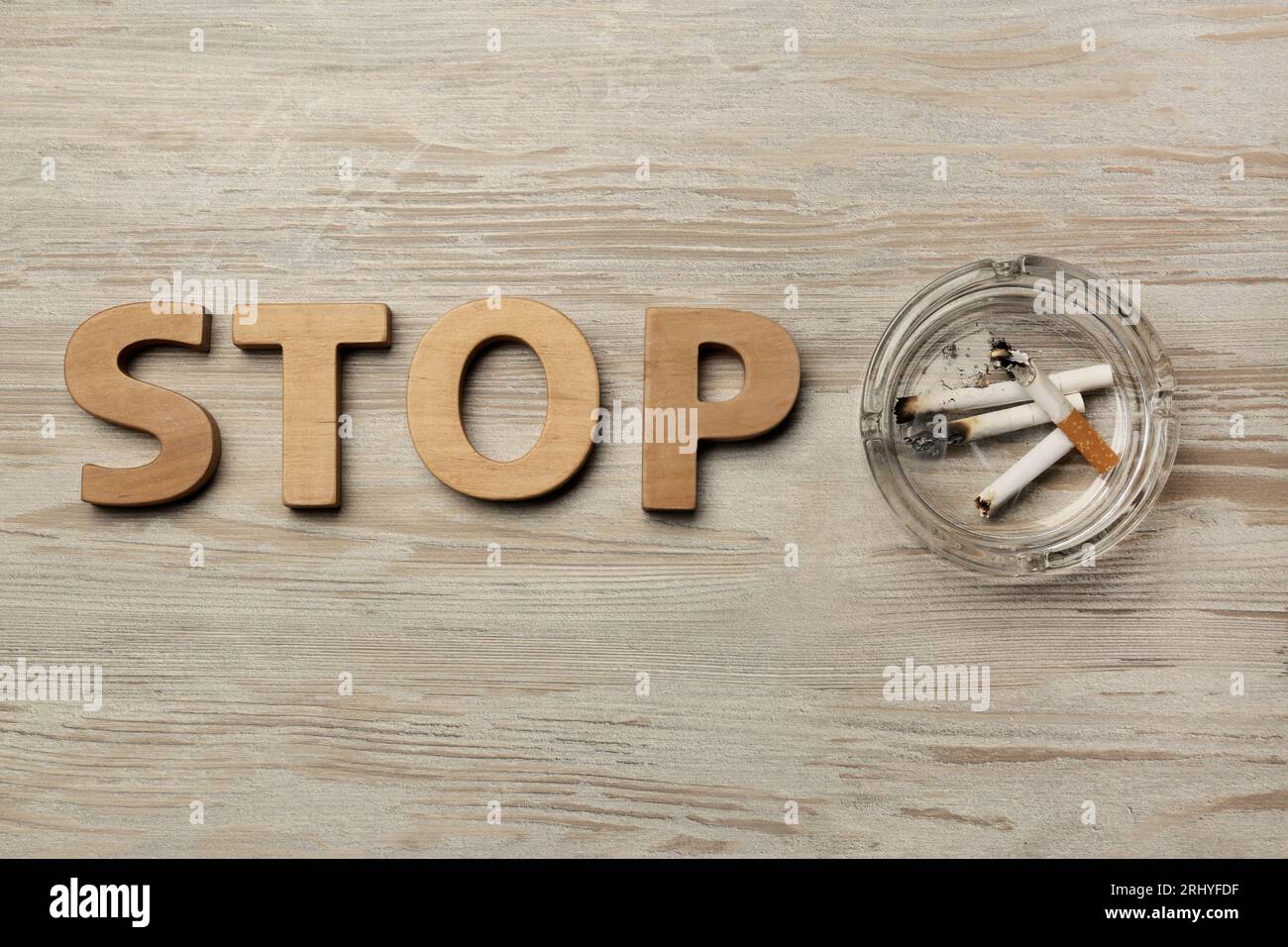 Ashtray with burnt cigarettes and word Stop made of letters on wooden ...