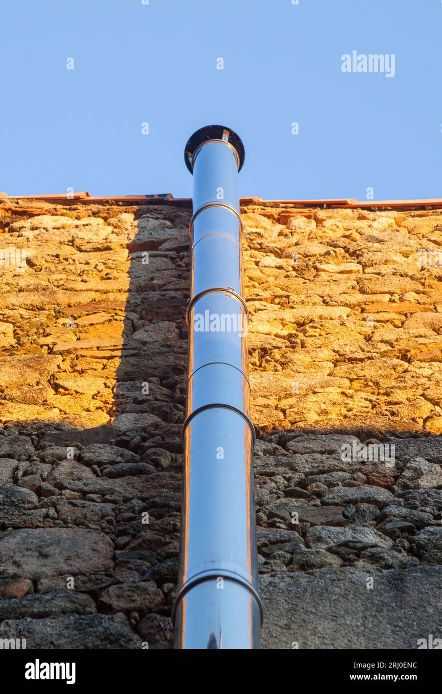 Chromed metal smokestack attached to a dry stone wall. Sunset light ...