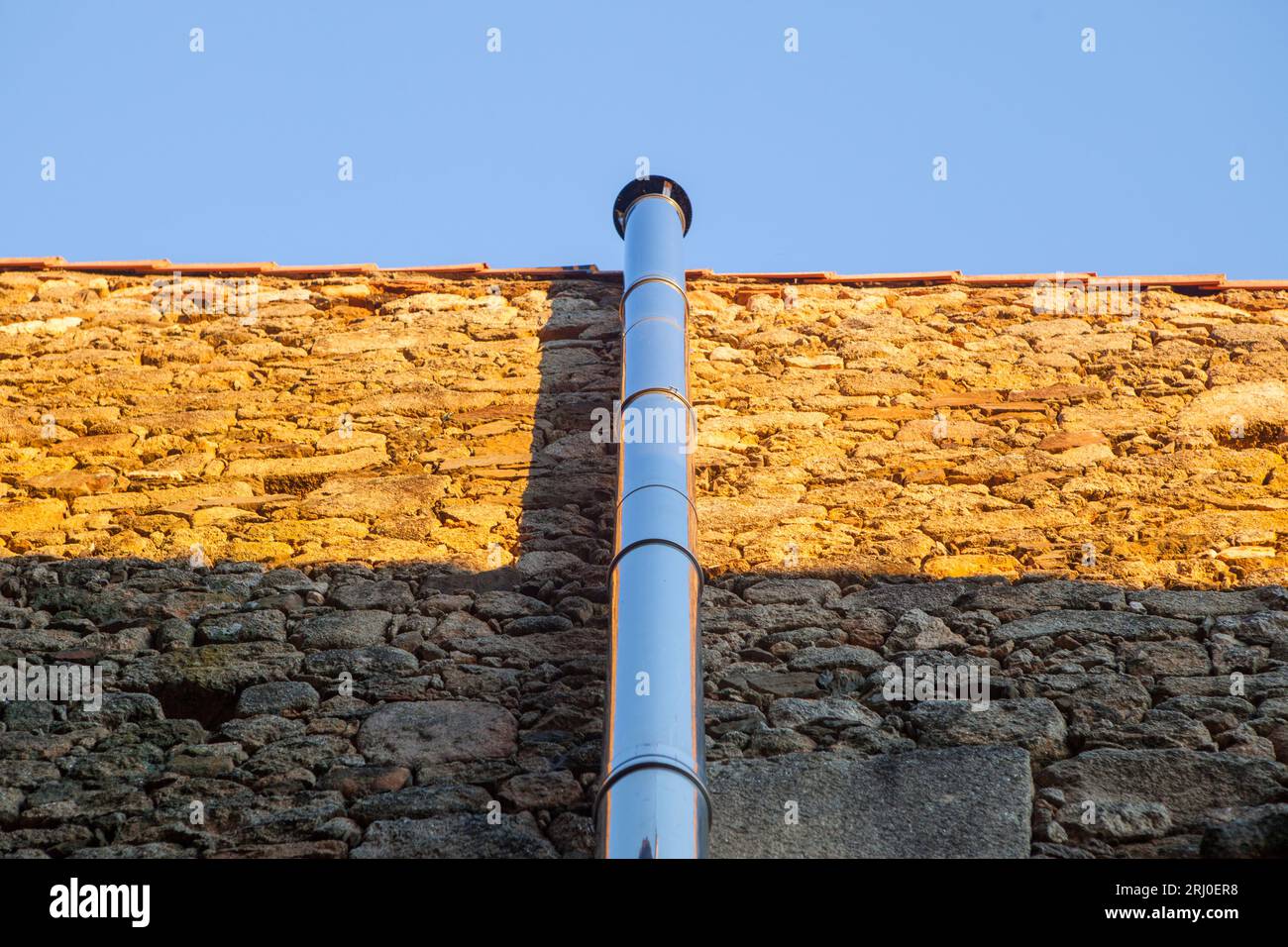 Chromed metal smokestack attached to a dry stone wall. Sunset light ...