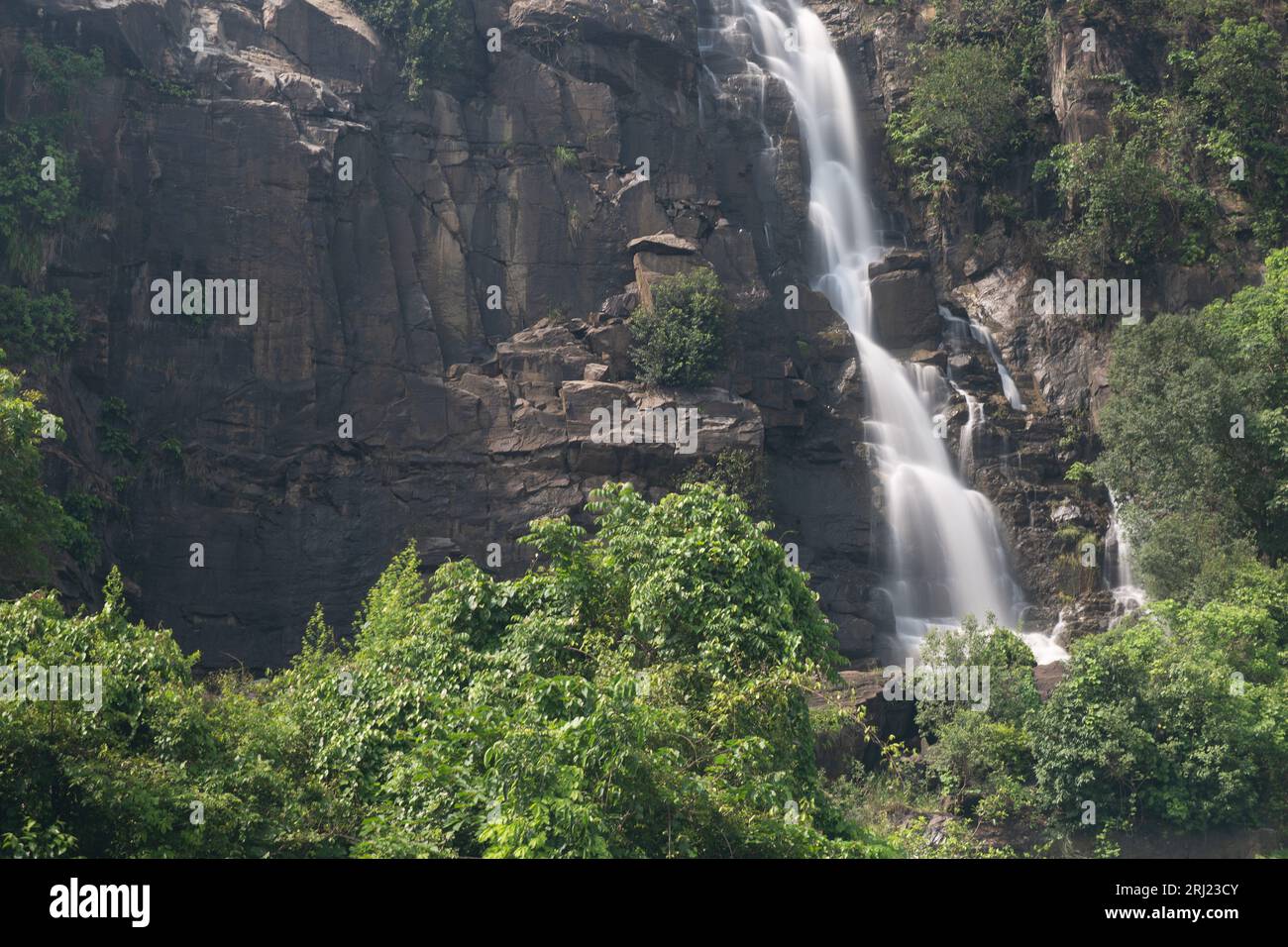 Silky milky smooth Sita waterfall flowing over green rocky hills at ...
