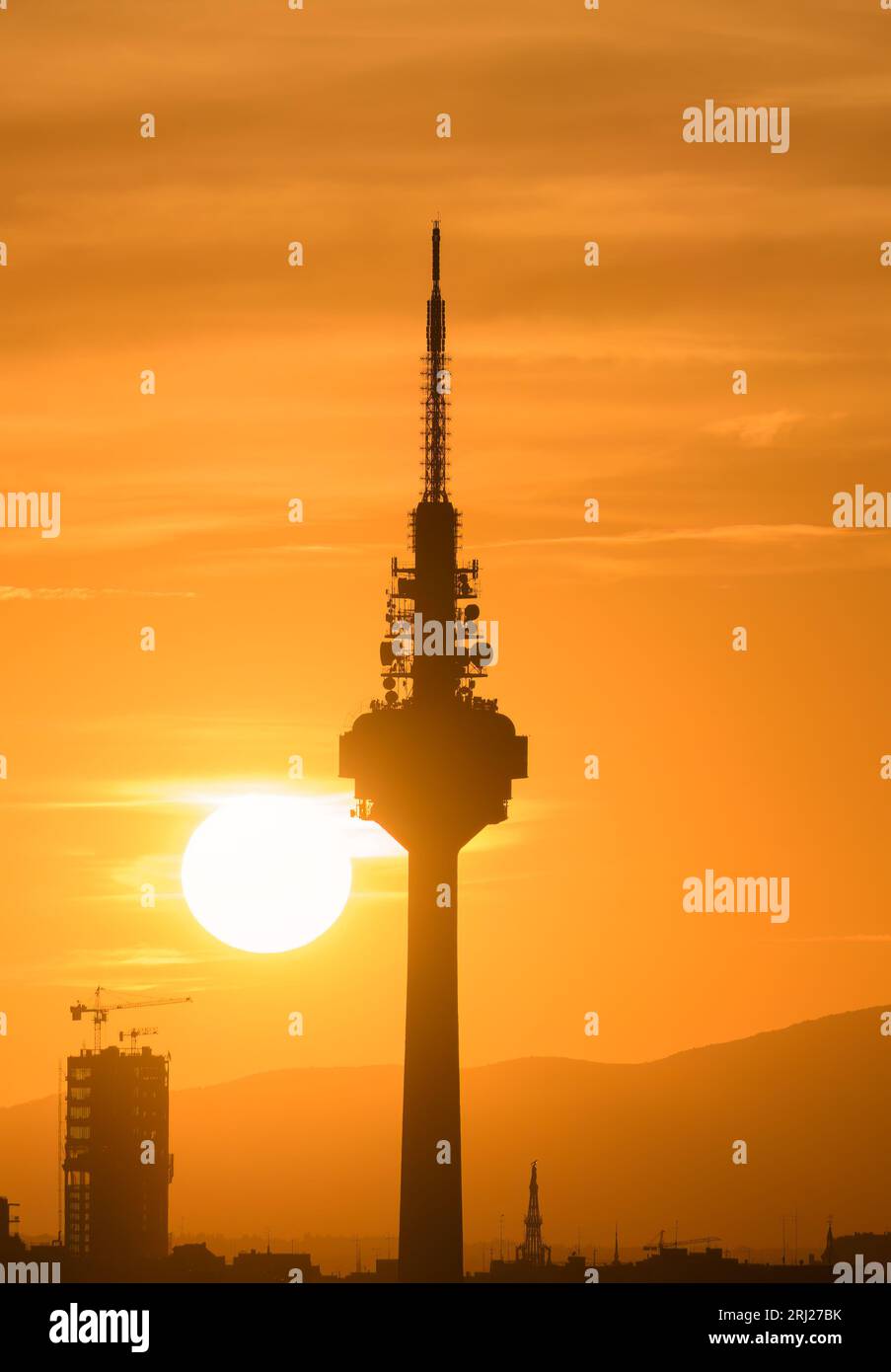 Sunset with the sun almost touching a communications tower. With clouds ...