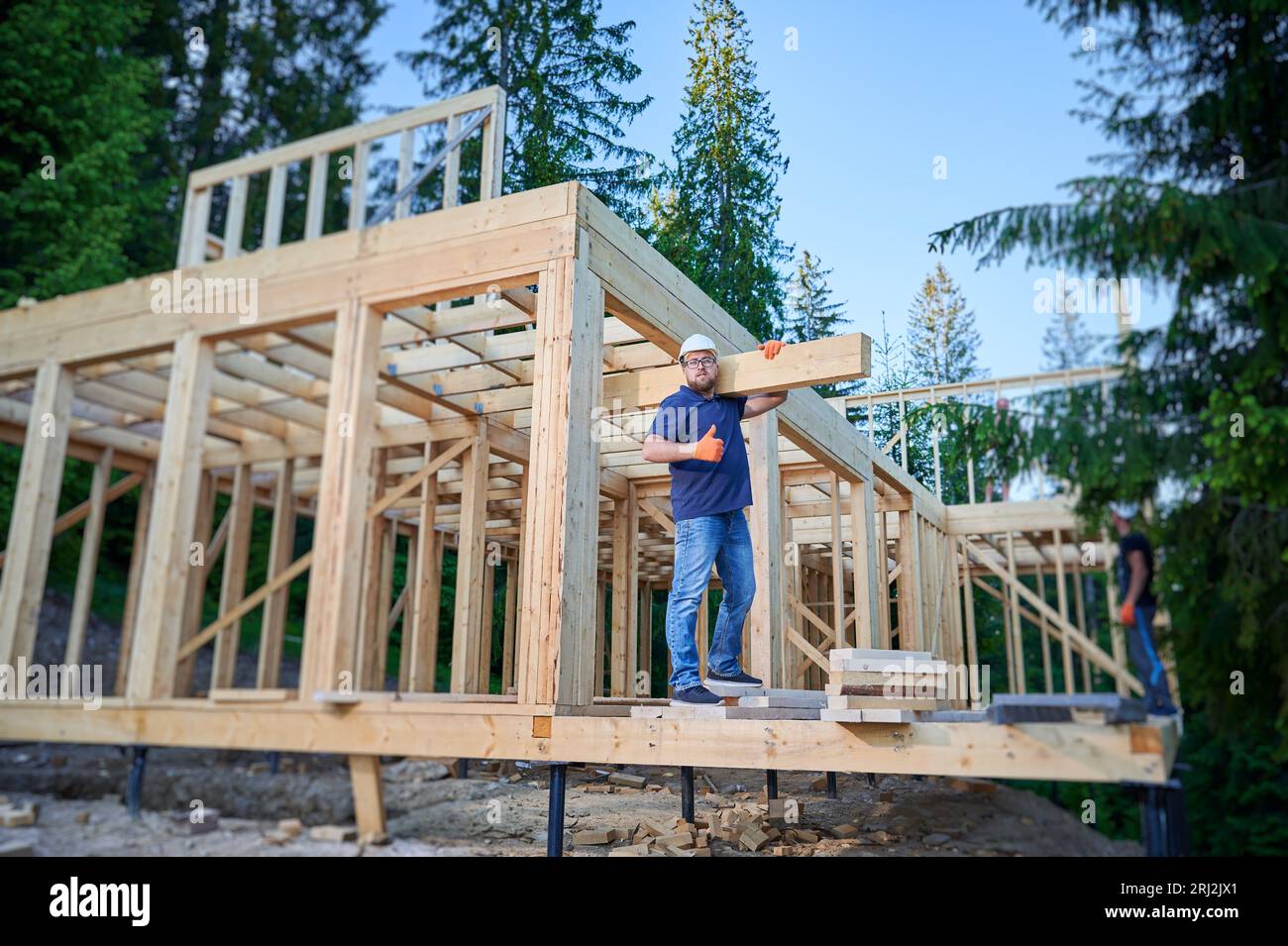 Carpenter builds wooden frame house near the forest. Bearded man holds ...