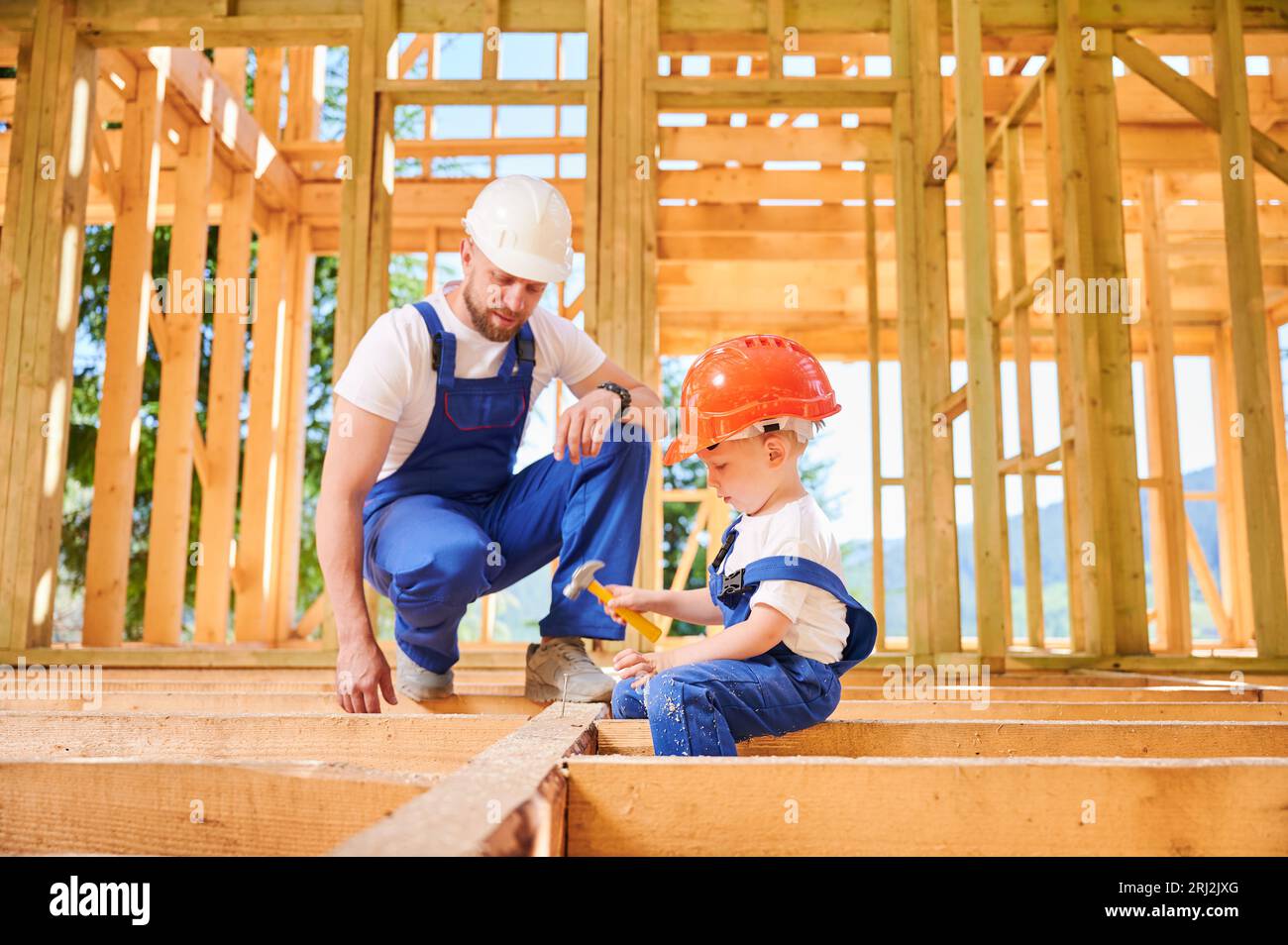 Father with toddler son building wooden frame house. Worker instructing ...