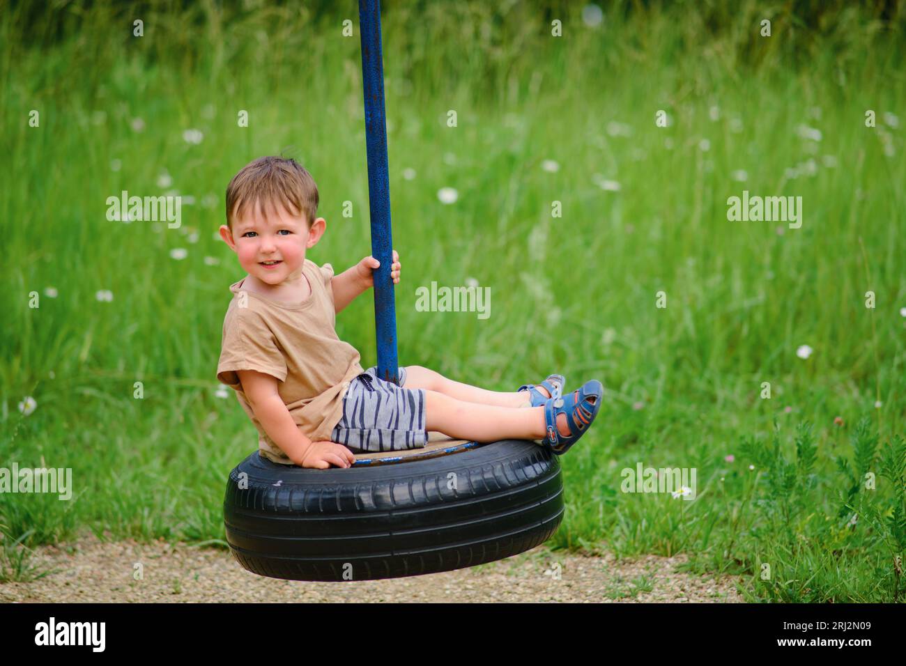 A smiling child enjoys playing on a car tire turned into a swing. A ...