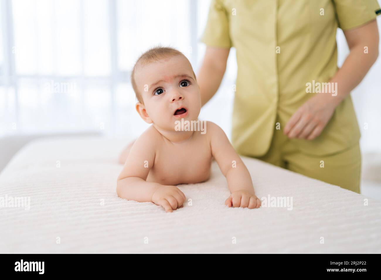 Front view of cute infant baby boy lying on belly while unrecognizable ...