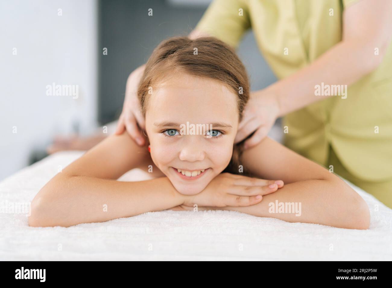 Portrait of adorable little girl having neck, shoulder and back massage ...