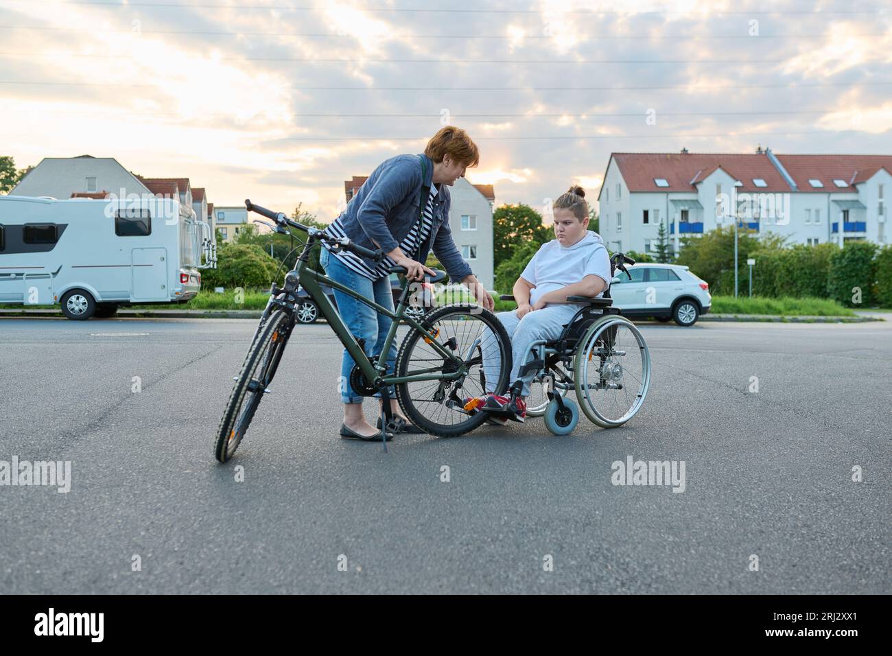 Disabled boy transfers from wheelchair to bicycle, mother helping child ...