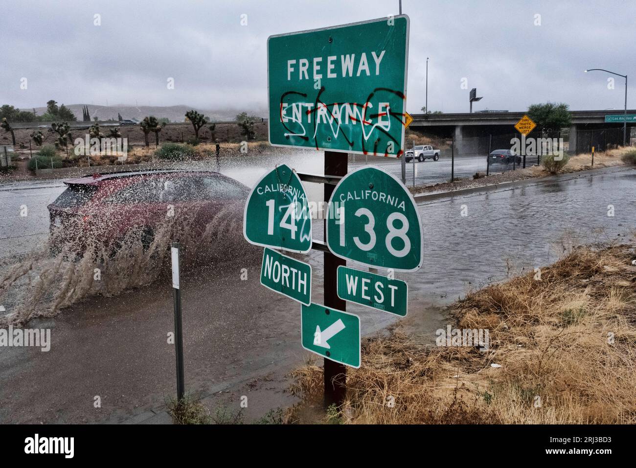 A vehicle engulfed in water drives through a flooded freeway entrance ...