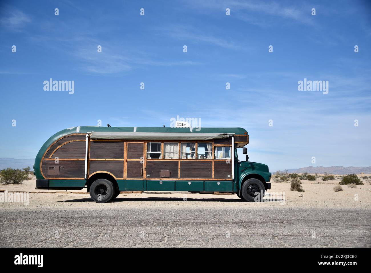 An aged green school bus on a dirt road in the desert against a blue ...