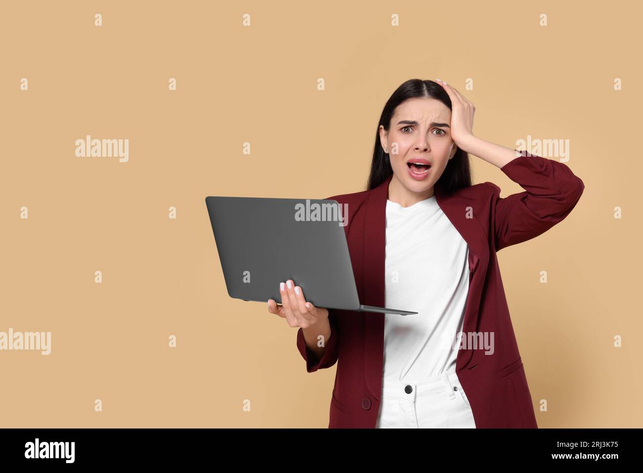 Shocked woman with laptop on beige background Stock Photo - Alamy