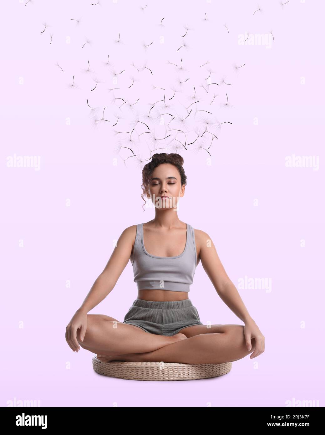 Beautiful young woman meditating on light pink background. Many dandelion seeds flying from her ...