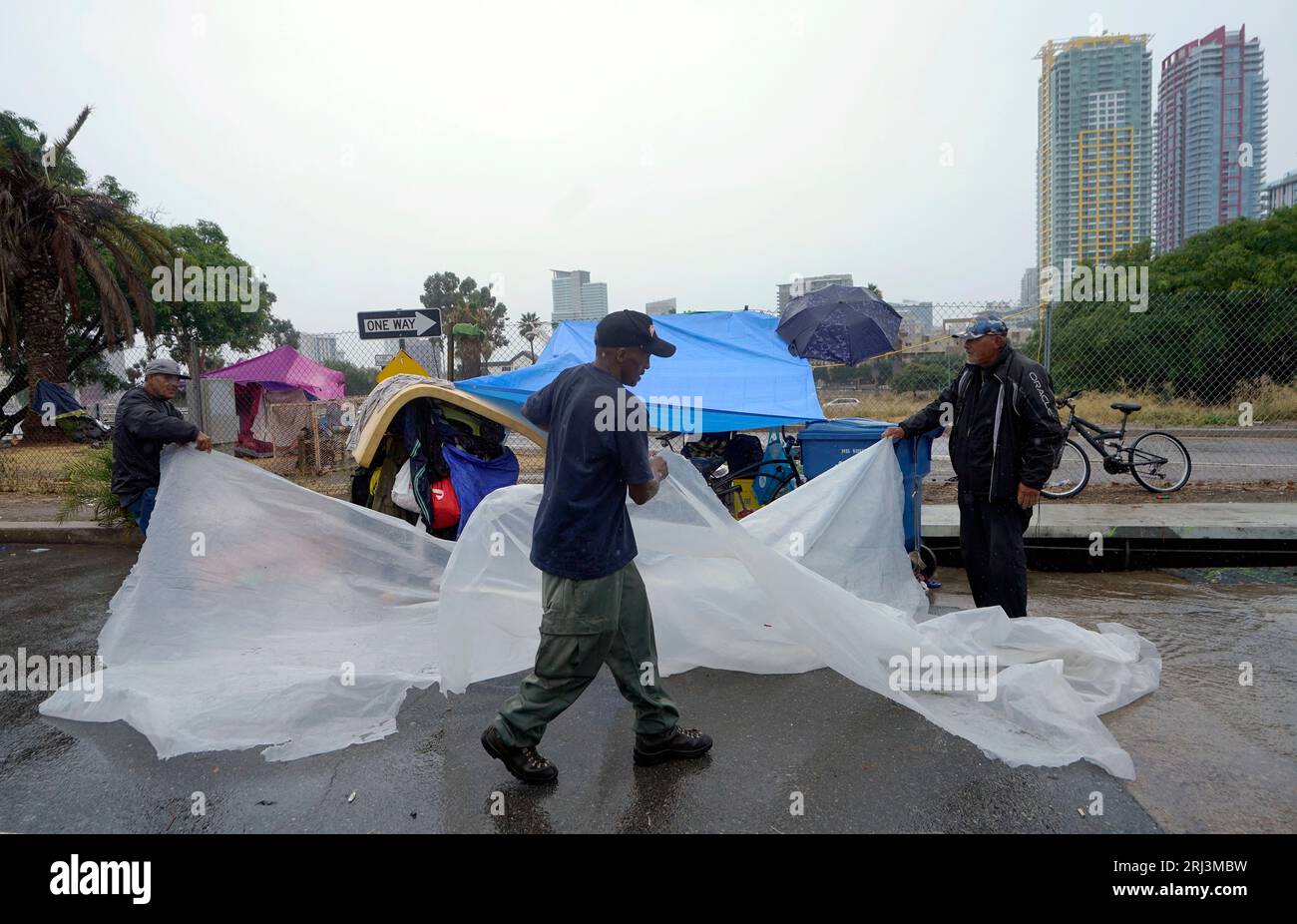 Homeless people carry a plastic tarp to shield themselves from a light ...