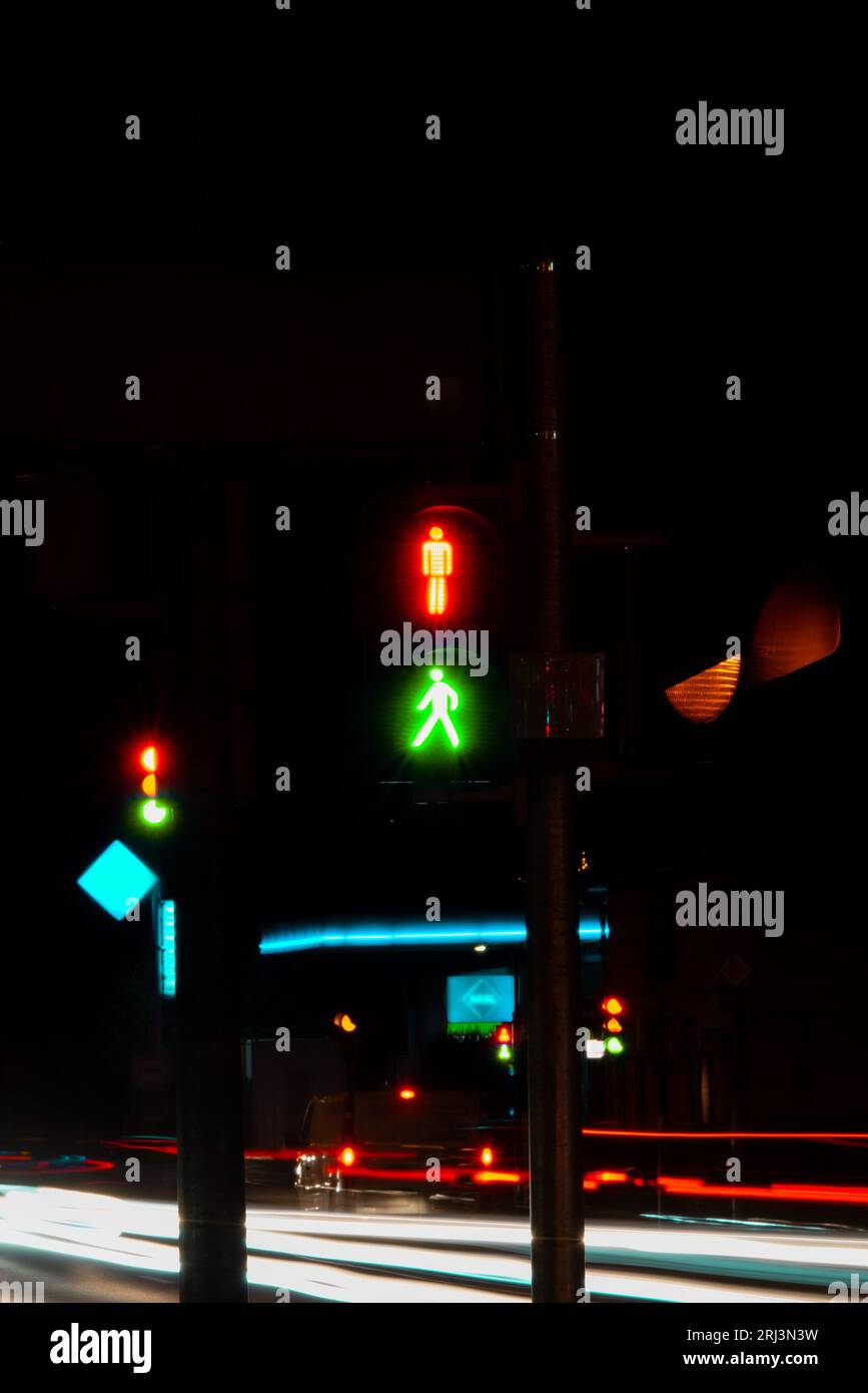 On a dark night, a row of cars drive past a traffic light with green ...