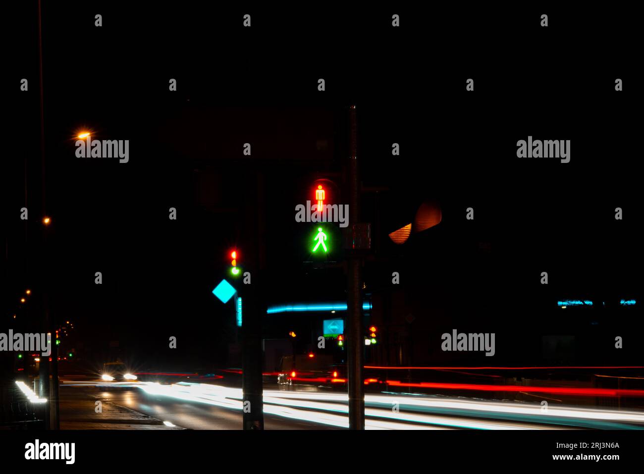On a dark night, a row of cars drive past a traffic light with green ...