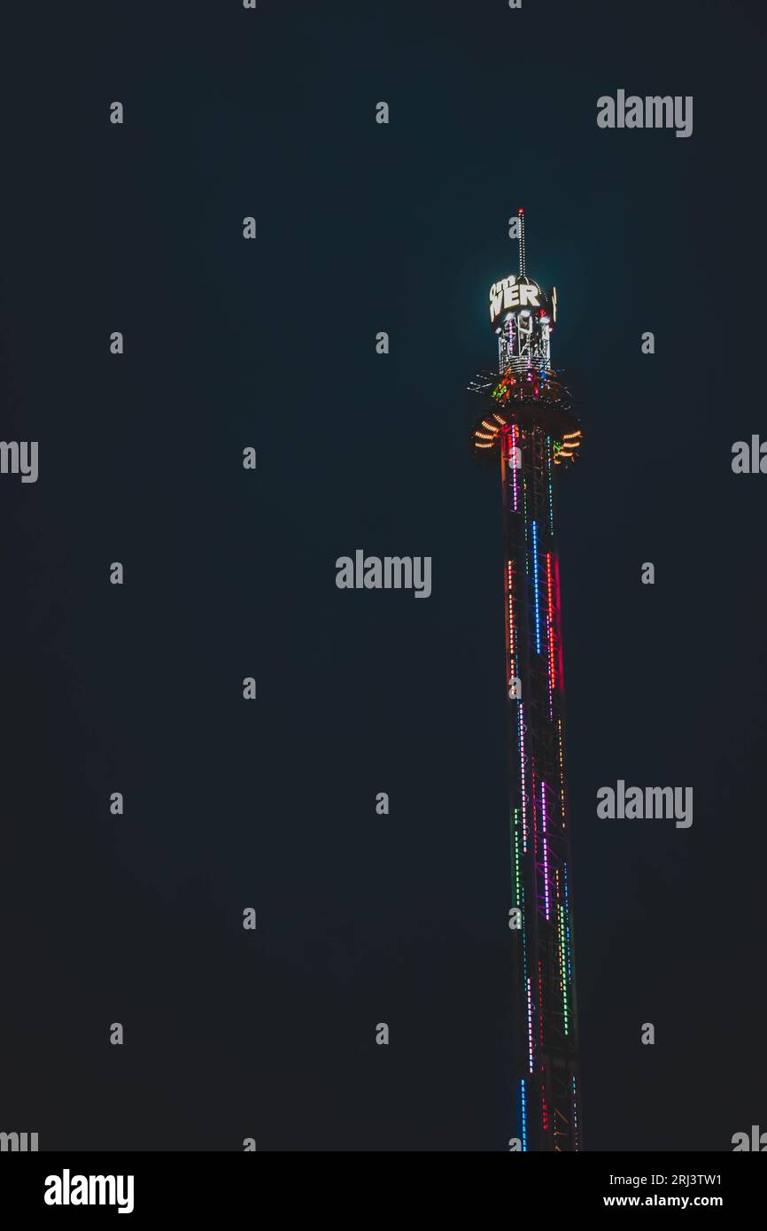 A scenic night-time view of a tall drop tower illuminated by a ...