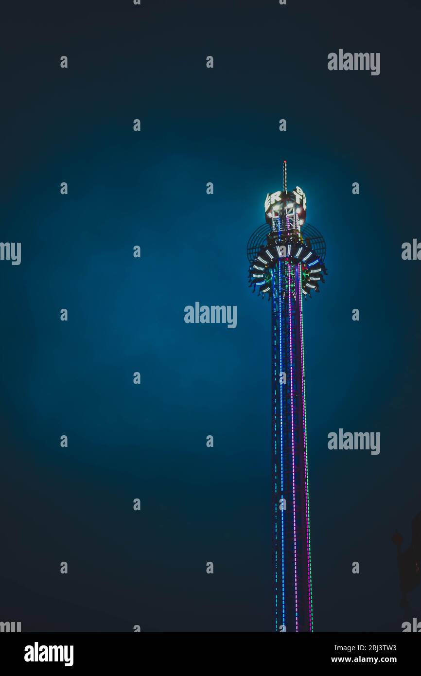 A scenic night-time view of a tall drop tower illuminated by a ...