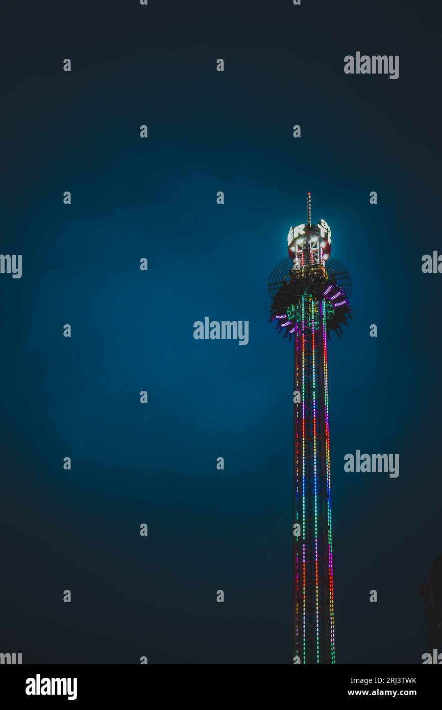 A scenic night-time view of a tall drop tower illuminated by a ...