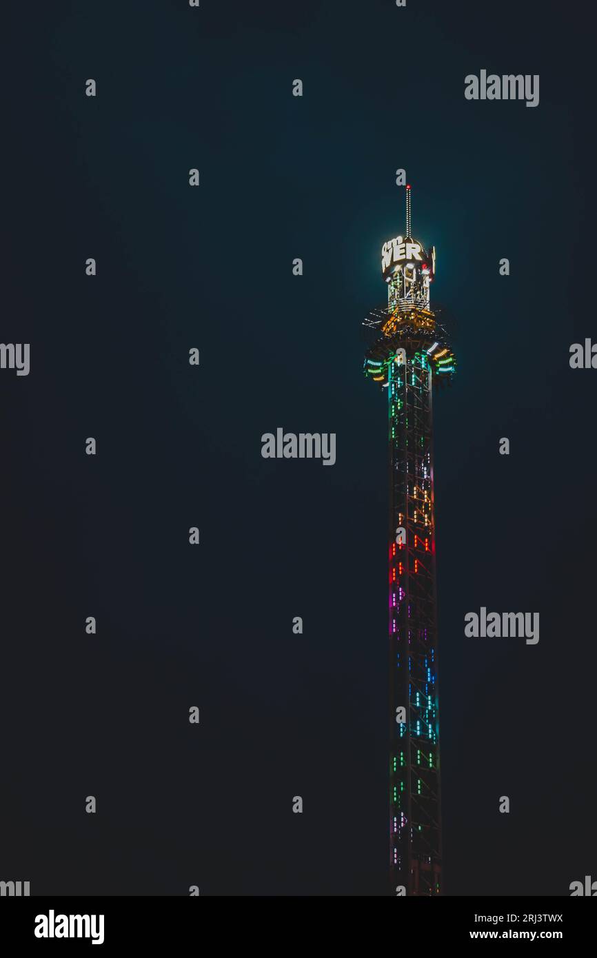 A scenic night-time view of a tall drop tower illuminated by a ...