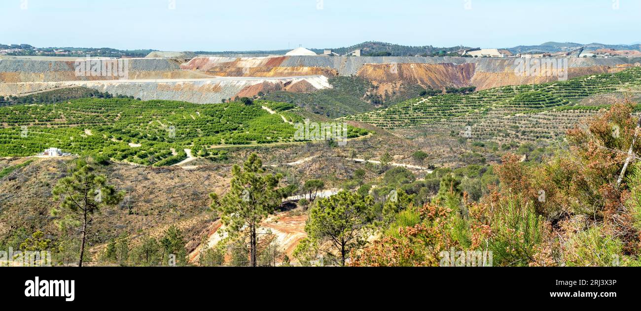 A vast expanse of an open-pit mine situated on a hillside covered in a ...